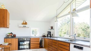 Uma cozinha com forno embutido, cafeteira e janela com vista para árvores.