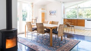 Uma área de jantar moderna com uma mesa grande, cadeiras de vime e uma lareira a lenha preta.