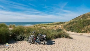 Uma bicicleta estacionada em um caminho de areia, com dunas e uma praia ao fundo.