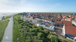 Uma cidade costeira com um calçadão, edifícios com telhados vermelhos e vista clara para o mar.