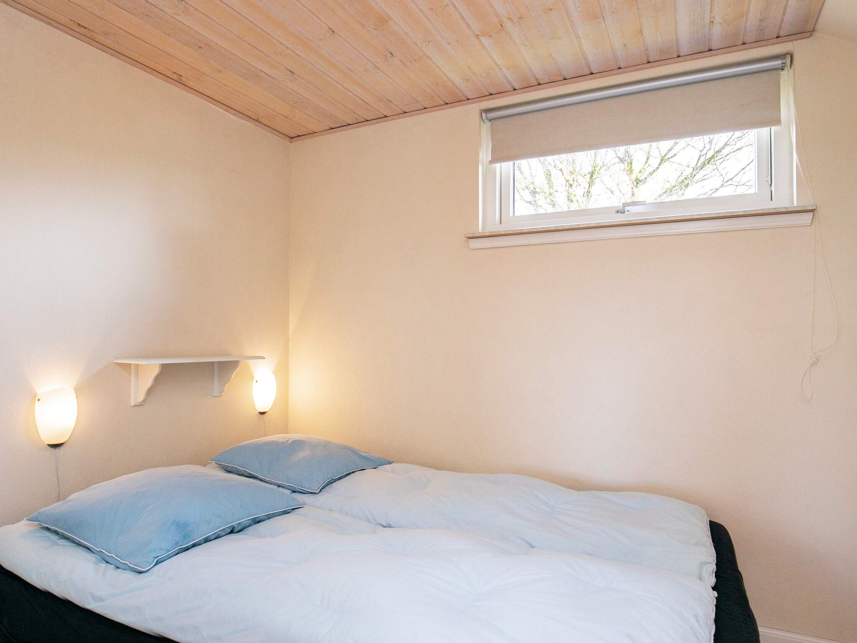 Quarto com cama, janela e luminárias fixadas na parede.
