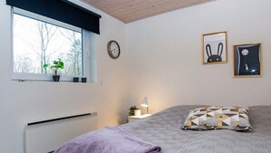 Quarto com cama, janela com plantas, relógio e duas imagens emolduradas na parede.