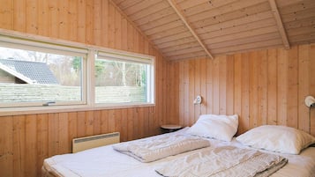 Quarto com paredes de madeira, cama com roupa de cama branca, uma janela e luminária fixada na parede.