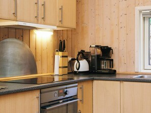 Cozinha com armários de madeira, fogão, chaleira e cafeteira.