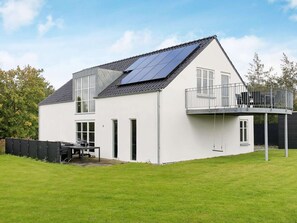 Uma casa moderna de dois andares com varanda, painéis solares e quintal cercado.