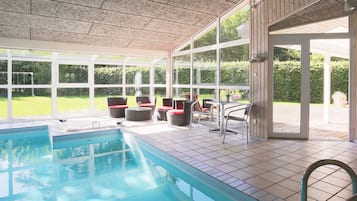 Área de piscina coberta ao ar livre com vista para um jardim e um pátio com mobiliário externo.