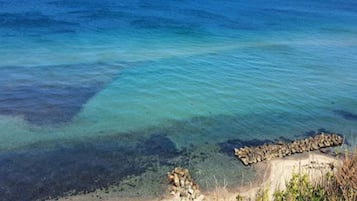Paisagem costeira com águas cristalinas, um afloramento rochoso e uma praia de areia.