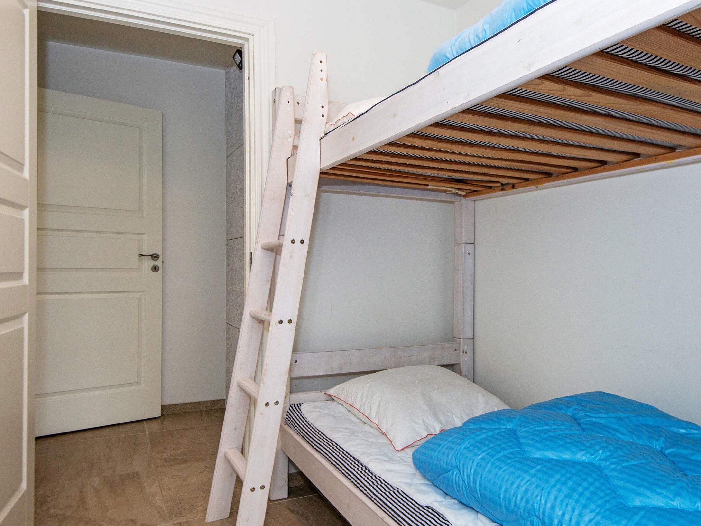 Uma cama de solteiro com escada de madeira, uma porta branca e um cobertor azul.