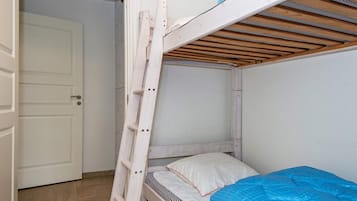 Uma cama de solteiro com escada de madeira, uma porta branca e um cobertor azul.