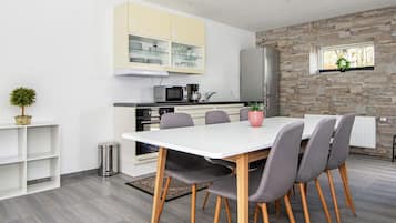 Cozinha moderna com uma mesa e cadeiras brancas, parede de pedra e uma janela.