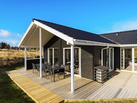 Uma casa moderna com um alpendre coberto, área de jantar com mobiliário para área externa e uma grande porta de vidro deslizante.