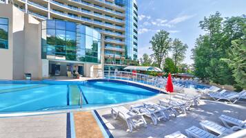Piscina com espreguiçadeiras e um edifício moderno com varandas.