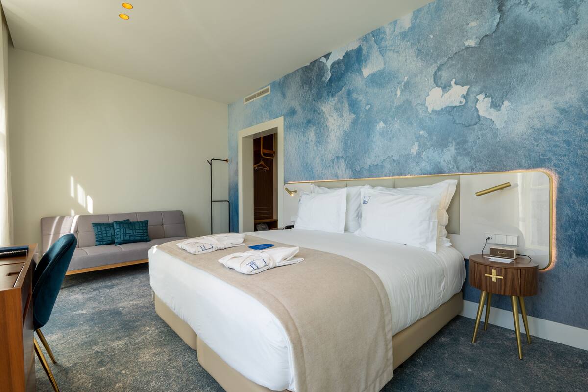 Quarto de hotel com uma cama grande, um sofá, uma escrivaninha e um guarda-roupa.