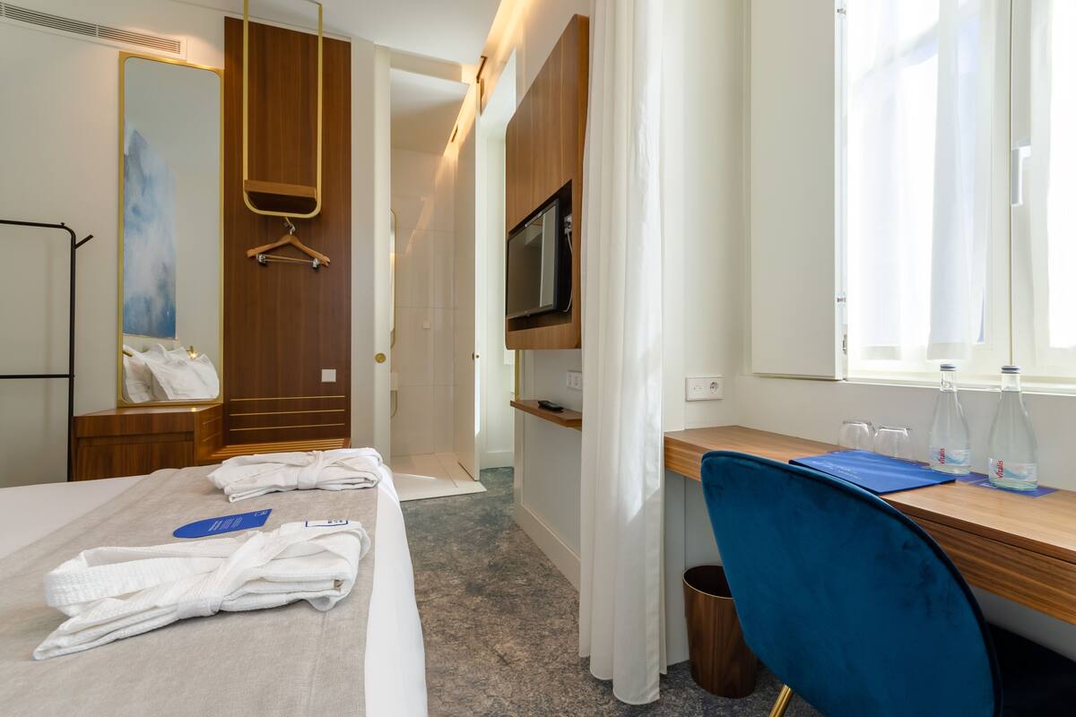 Quarto de hotel com cama, escrivaninha, cadeira, televisão, espelho e janela com cortinas.