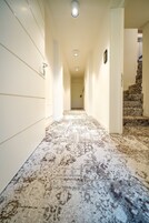 Um corredor com carpete estampado, paredes brancas e escada com carpete padronizado.