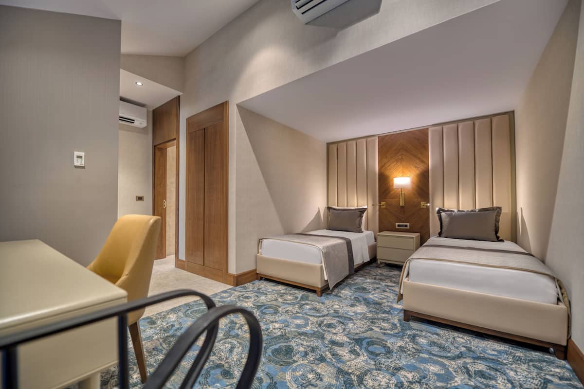 Quarto de hotel com cama, duas mesas de cabeceira, escrivaninha e uma cadeira.