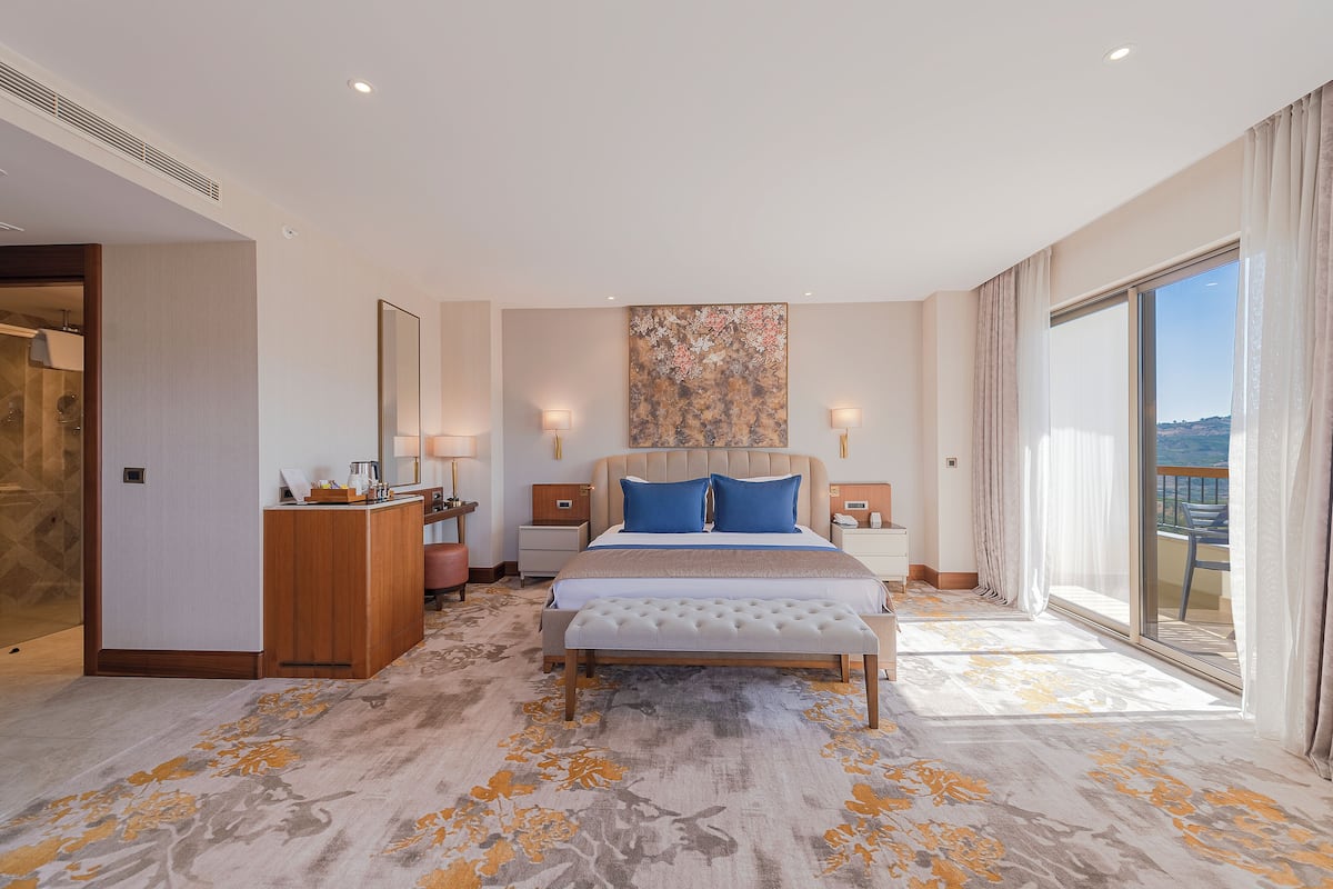 Quarto de hotel espaçoso com uma cama grande, varanda com vista e um painel decorativo.