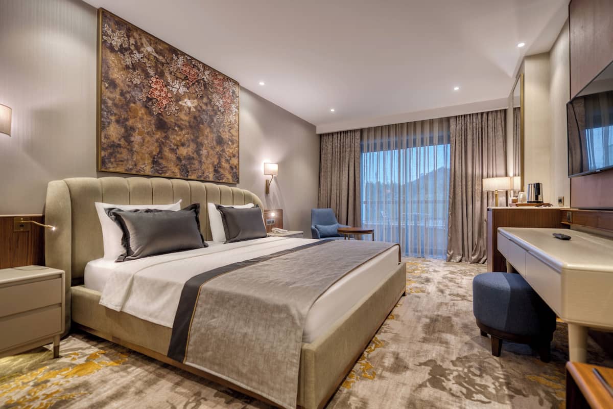 Quarto de hotel com uma cama grande, uma escrivaninha, uma cadeira, uma televisão e um quadro na parede.