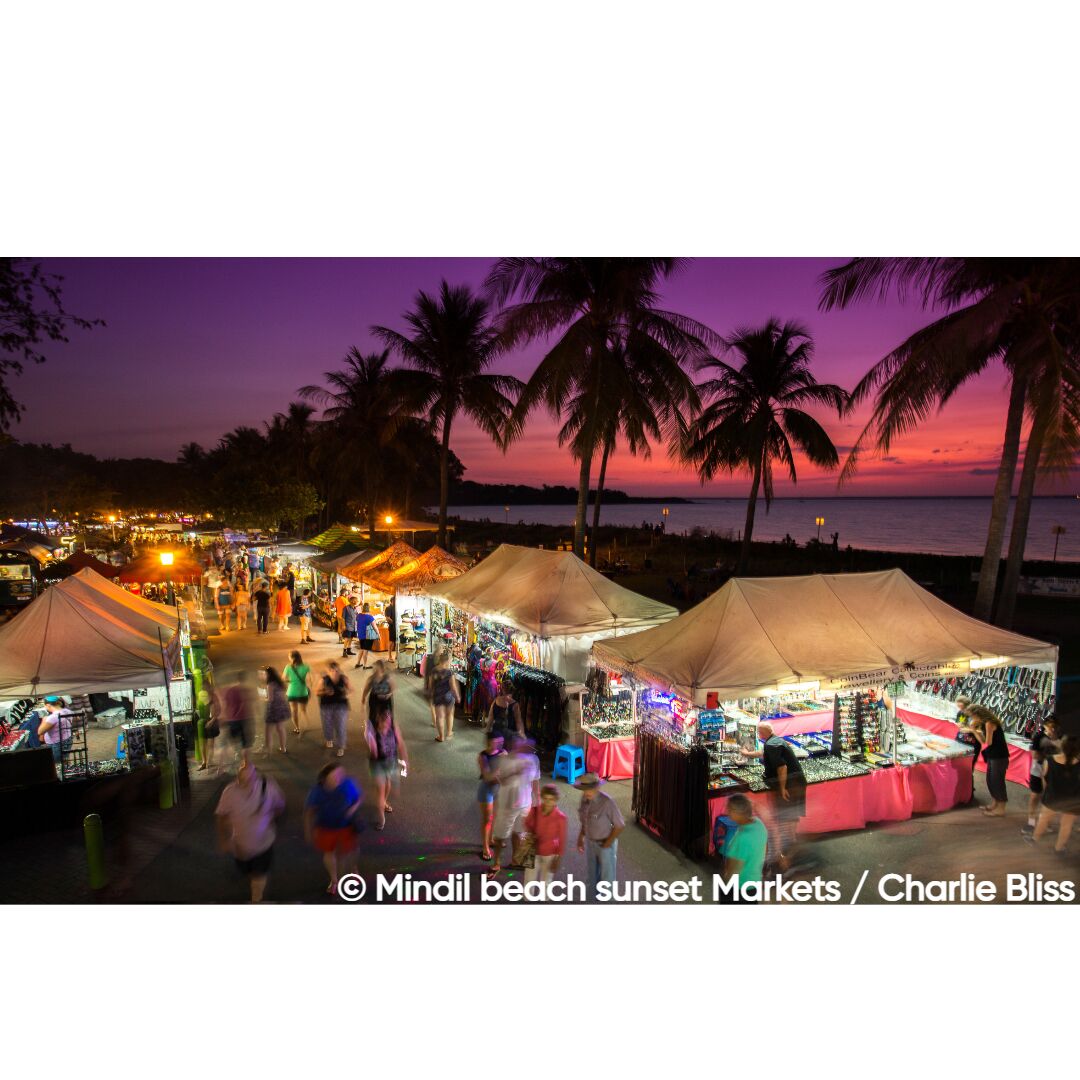 Mercado de praia ao pôr do sol, com toldos e pessoas.