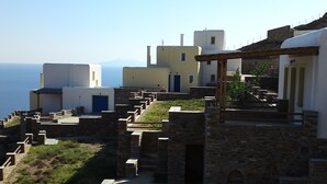 Uma vila costeira com edifícios de pedra tradicionais, alguns com portas azuis, e vista clara para o mar.