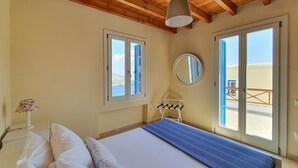 Quarto com cama, luminária, espelho e vista da praia através de amplas janelas.