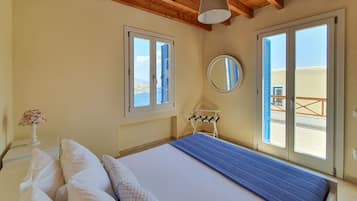 Quarto com cama, luminária, espelho e vista da praia através de amplas janelas.