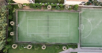 Vista aérea de uma quadra de tênis com vegetação ao redor e uma quadra de basquete.