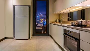 Cozinha moderna com forno embutido, geladeira e vista para a cidade à noite.