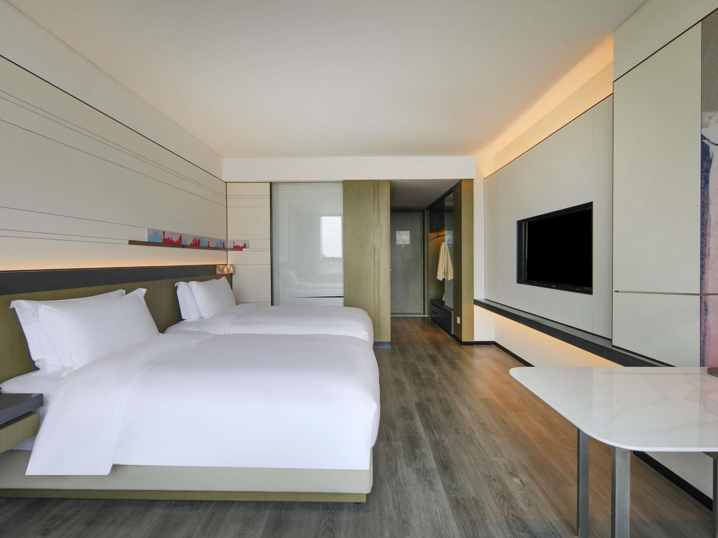 Quarto de hotel com cama, televisão, escrivaninha e guarda-roupa.