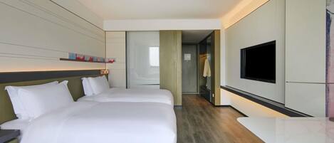 Quarto de hotel com cama, televisão, escrivaninha e guarda-roupa.