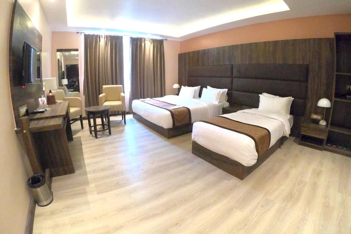 Quarto de hotel com duas camas, uma mesa, uma cadeira, uma televisão e uma estante de livros.