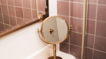 Um banheiro com um espelho redondo fixado numa parede branca, base dourada e padrão de azulejos xadrez ao fundo.