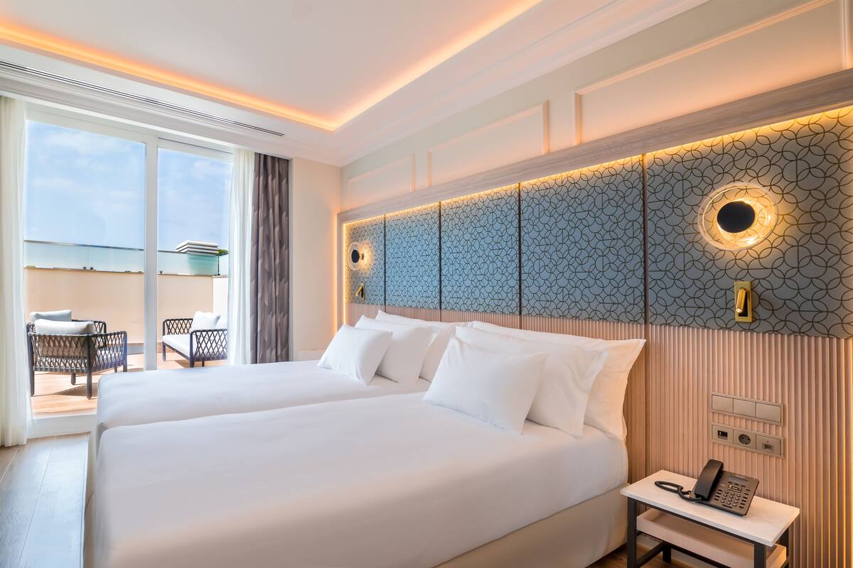 Quarto de hotel com uma cama grande, uma mesa de cabeceira com telefone e vista para a varanda.