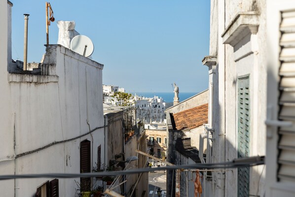 Uma rua estreita com edifícios brancos, uma estátua e vista para o mar.