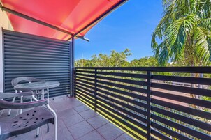 Varanda com toldo vermelho, grade de metal e mesa com cadeiras.