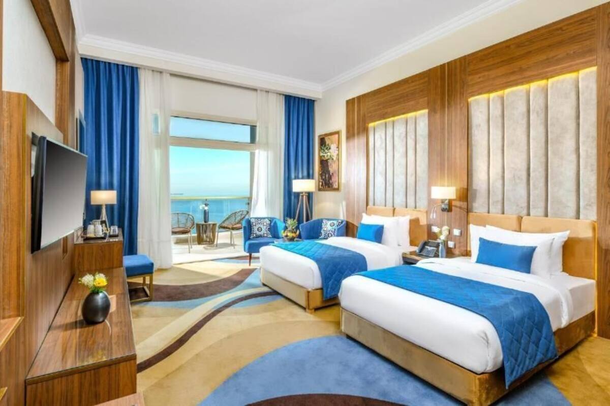 Quarto de hotel com duas camas, televisão, secretária e vista para o mar.