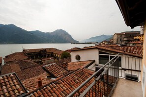 Um terraço com telhas de barro, uma janela redonda e vista para um lago e montanhas.