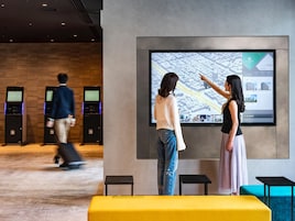 Um saguão moderno com um grande painel de mapa interativo, áreas de estar e totens de autoatendimento.