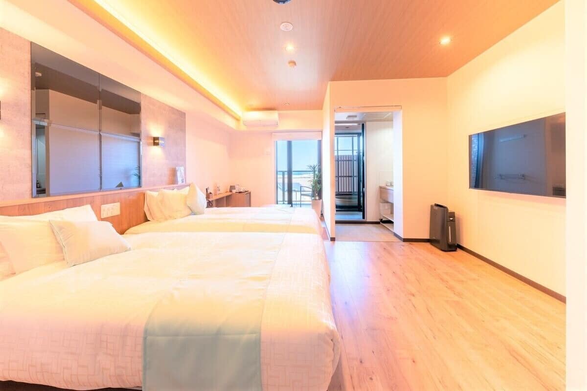 Quarto de hotel moderno com duas camas, uma TV grande e uma varanda com vista.