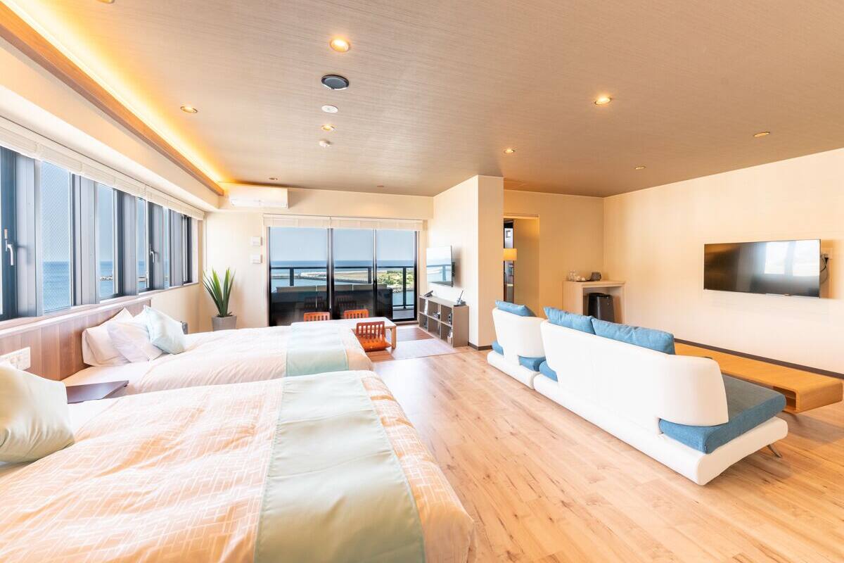 Quarto de hotel moderno com duas camas, um sofá, uma TV e uma varanda com vista.