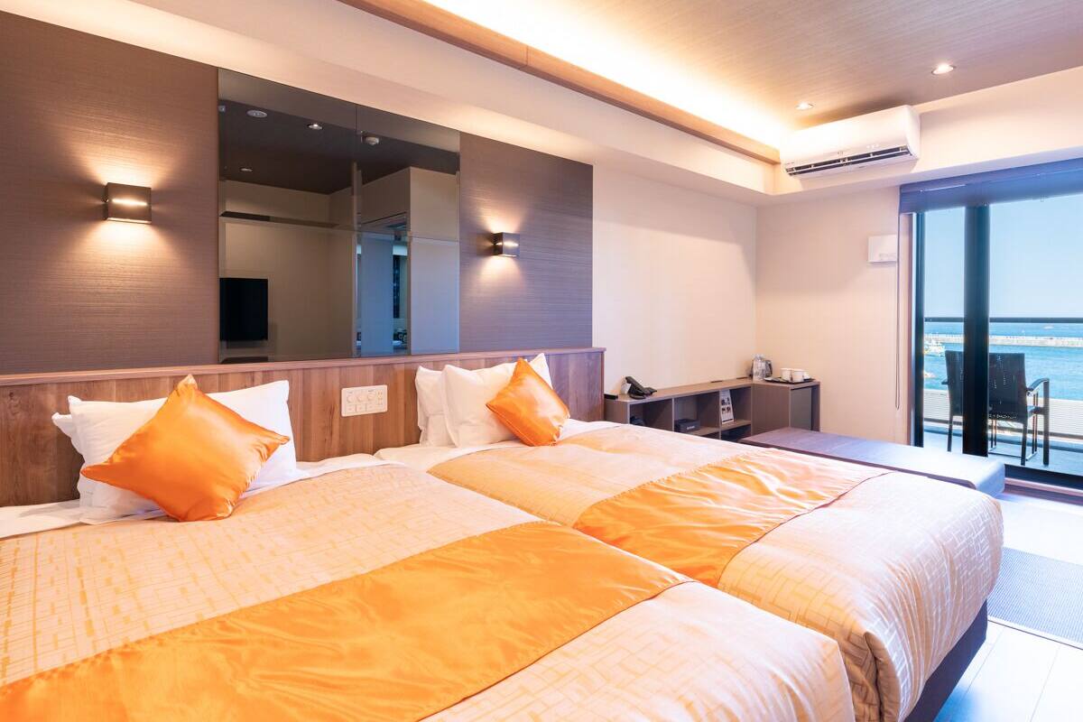 Quarto de hotel com duas camas, uma mesa de trabalho e uma janela grande com vista para o mar.