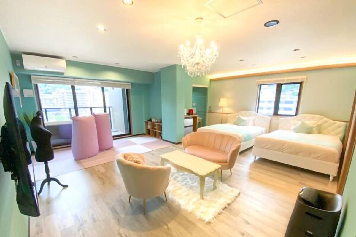 Quarto de hotel moderno com cama, sofá, poltrona, mesa pequena e lixeira.
