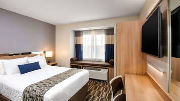 Quarto de hotel com uma cama grande, uma escrivaninha, uma cadeira, televisão de tela plana, janela com cortinas e televisão na parede.