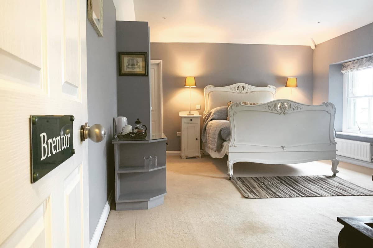 Quarto com cama, mesas de cabeceira, cômoda e porta com a inscrição 'Brentor'.