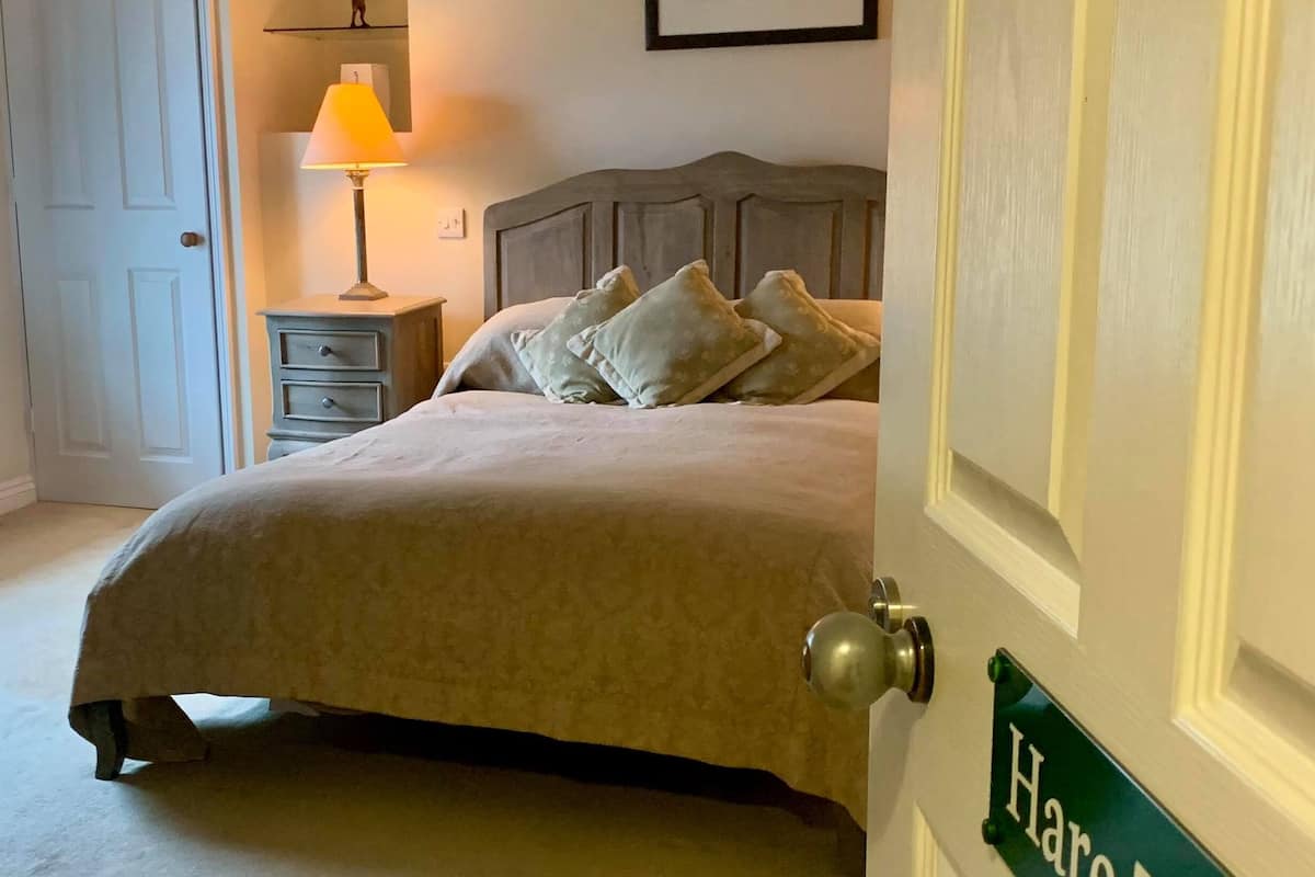 Quarto com cama, mesa de cabeceira, abajur e quadro na parede.