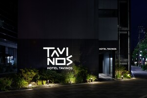 Um edifício moderno com uma placa chamativa para 'TAVINOS HOTEL TAVINOS' à noite.