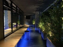 Um corredor moderno com paredes de vidro, um elemento aquático iluminado em azul e um jardim vertical.