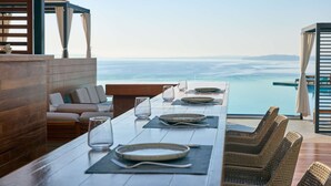 Uma área de refeições com vista para o mar, com uma mesa de madeira, cadeiras de vime e um sofá.