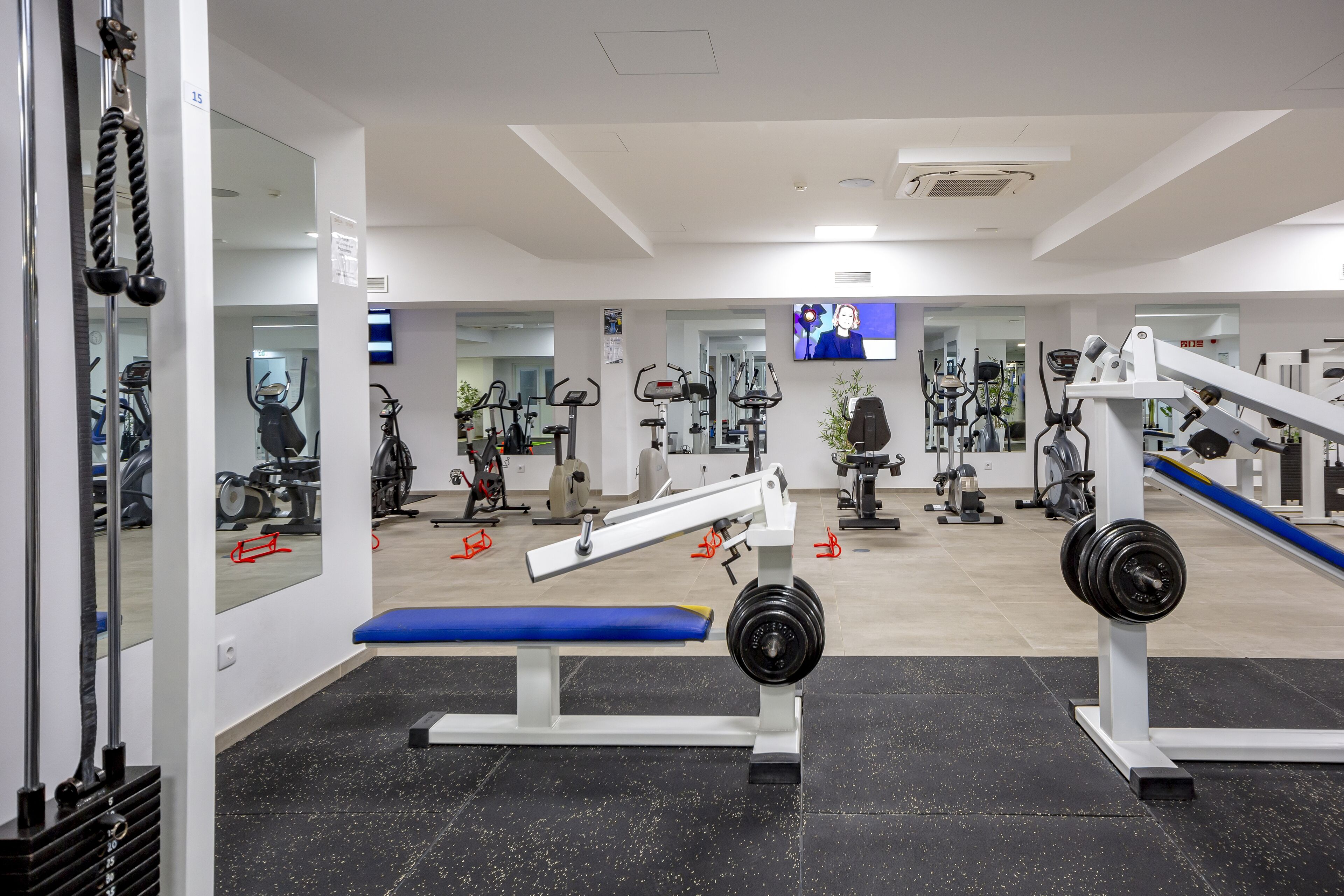 Uma academia com diversos equipamentos de ginástica, incluindo um banco, banco de musculação e aparelhos cardiovasculares.