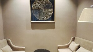 Um quarto com dois sofás bege, uma mesa redonda preta e uma obra de arte abstrata na parede.